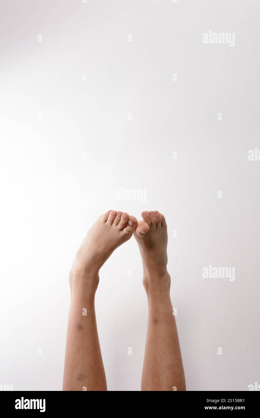A pair of legs are raised against a plain white background. The feet ...