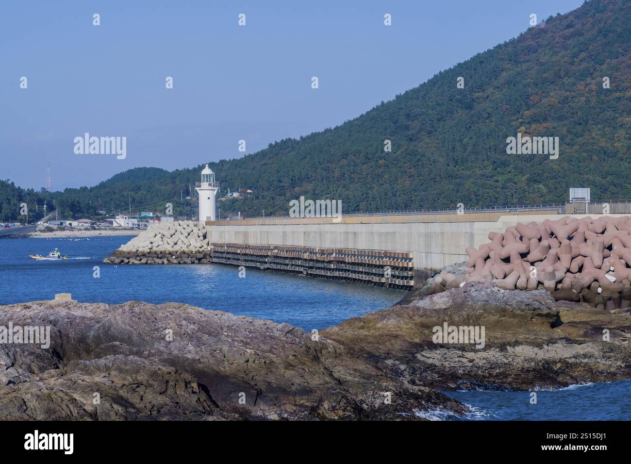 A lighthouse on a seawall with rocky foreground and hills in the ...
