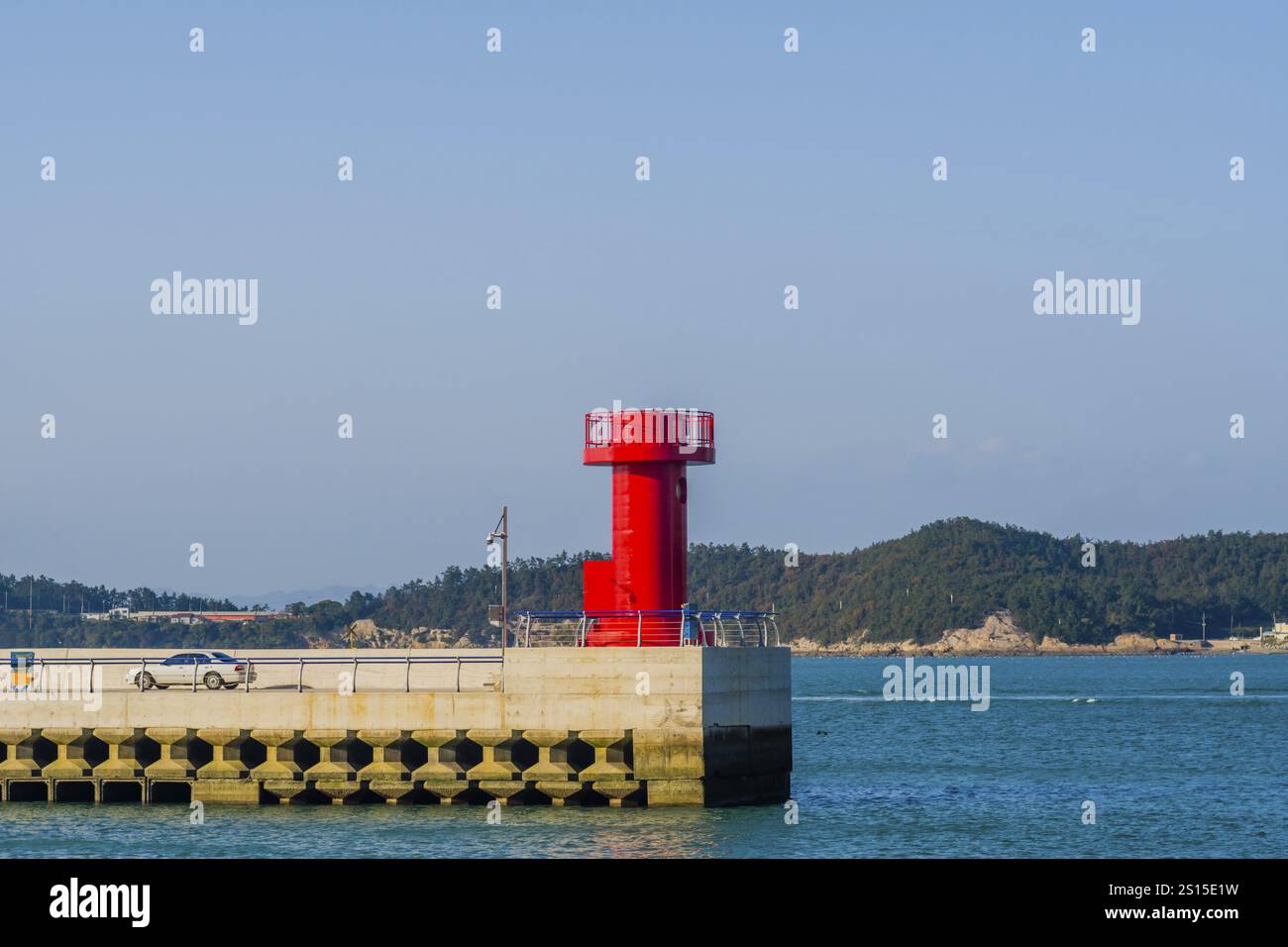 A red lighthouse on a pier with calm waters and blue skies, located in ...