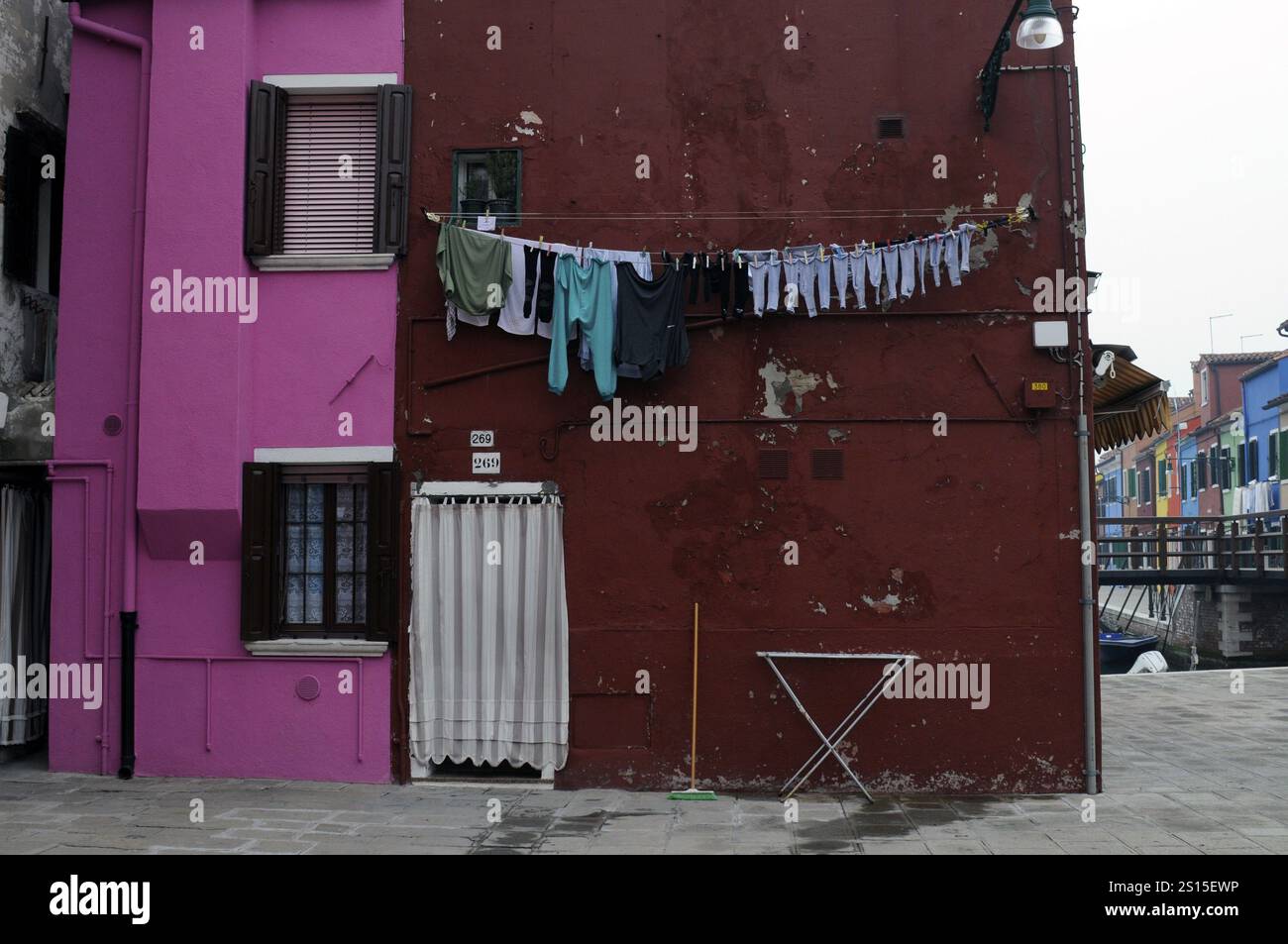 Small window and clothesline with colourful clothes on a dark red wall ...