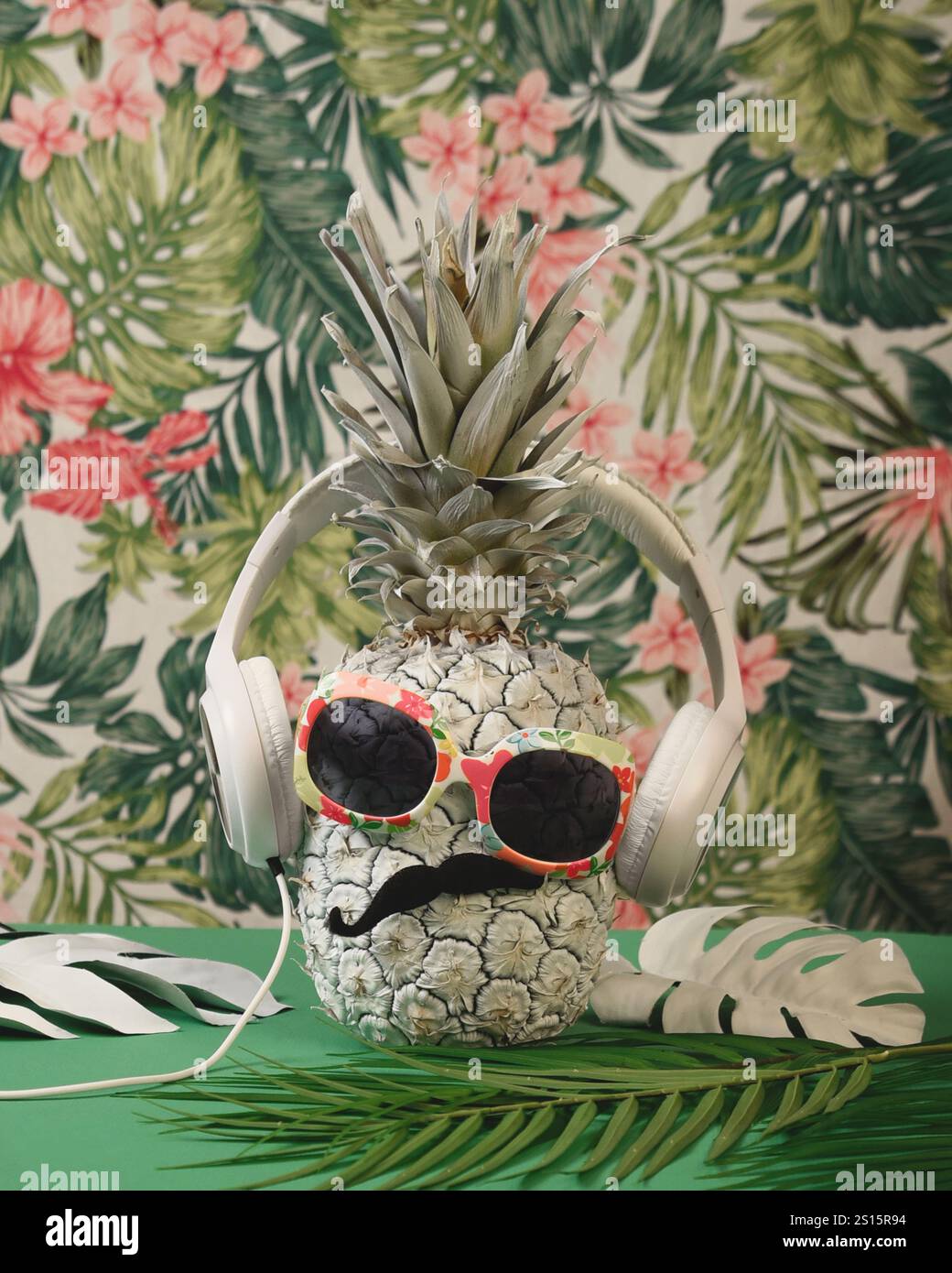 A pineapple is wearing music headphones with a moustache on a tropical ...