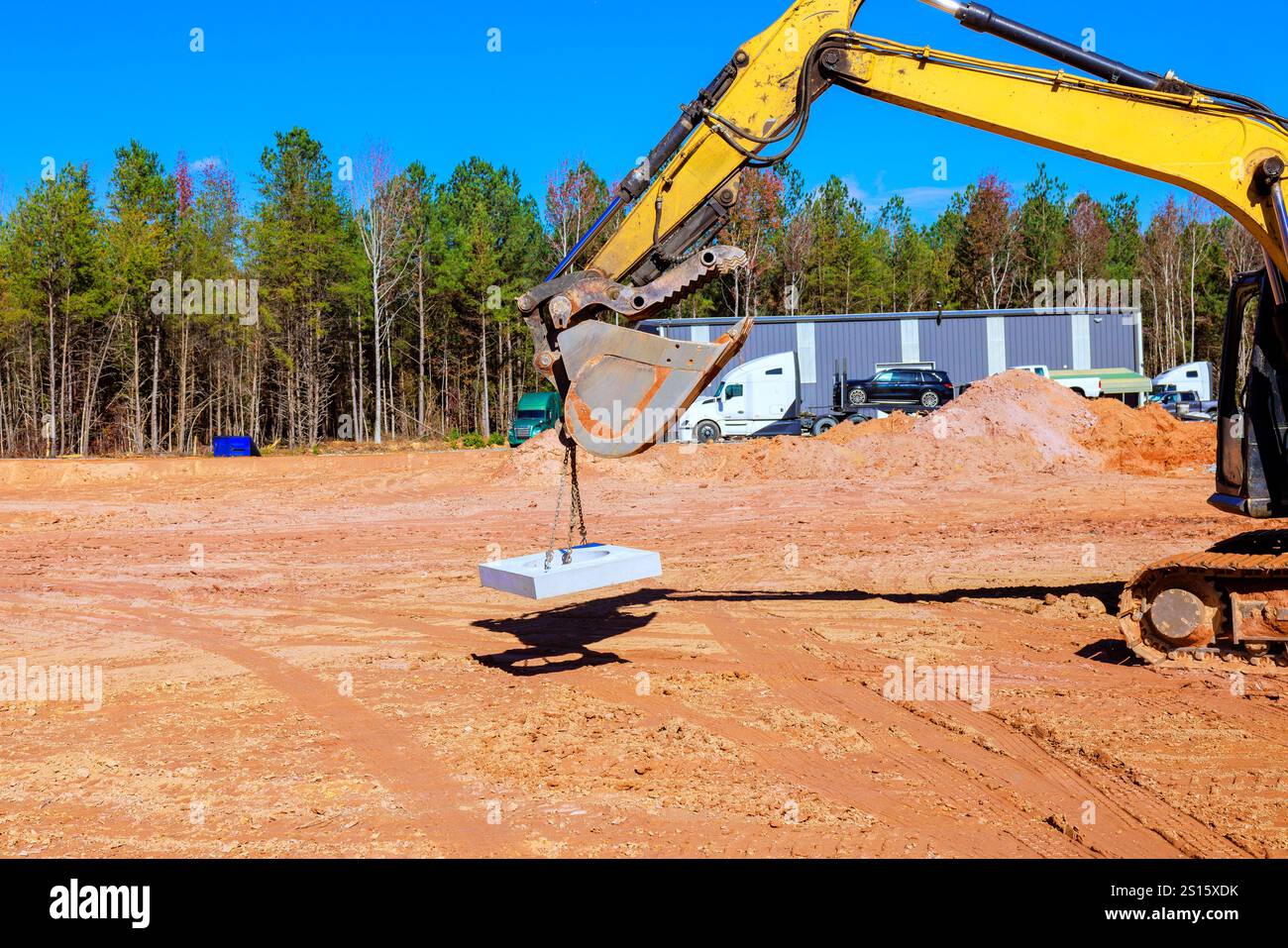 Excavator lifts concrete slab at construction site with trucks storage ...