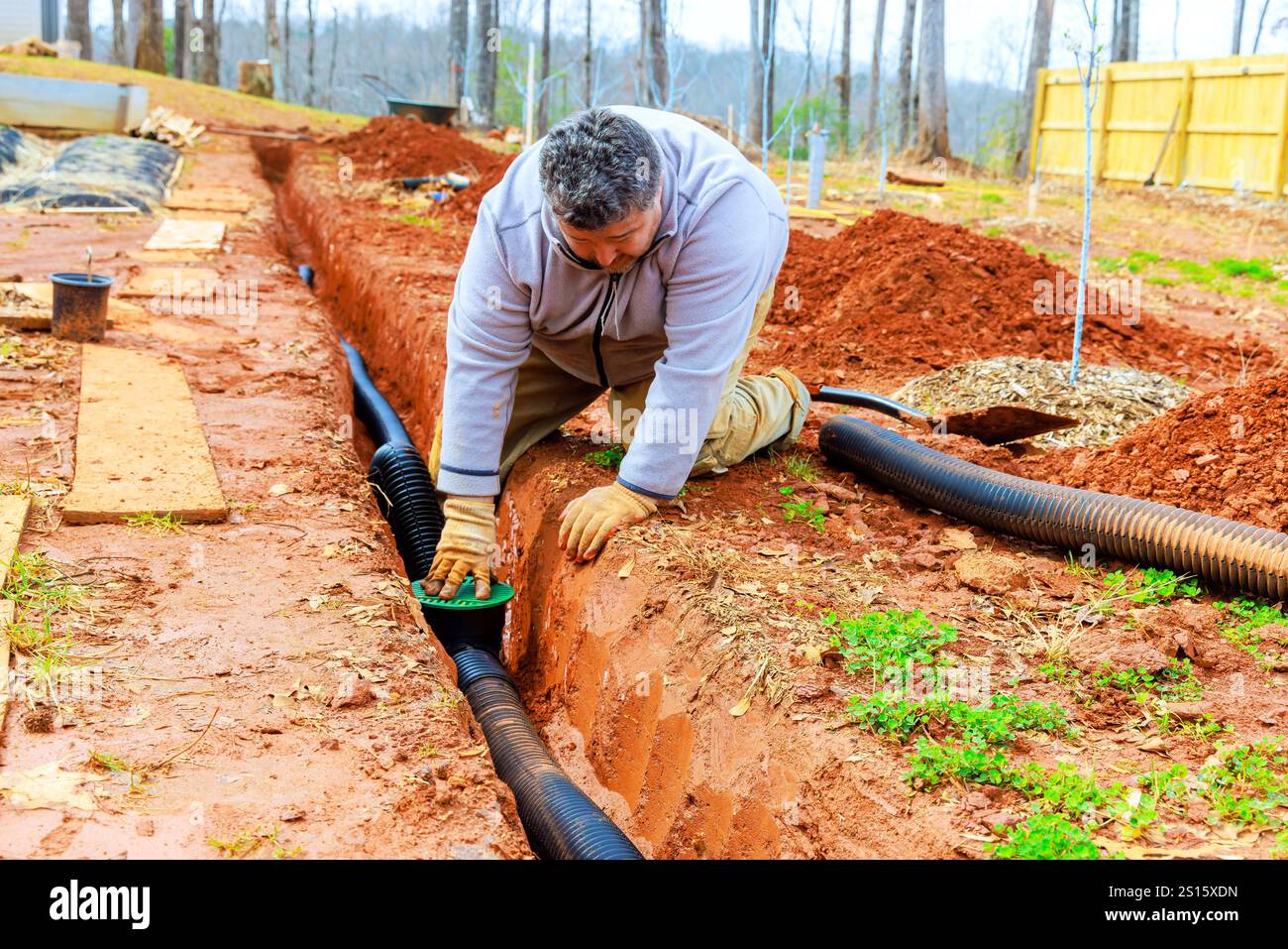 Man works diligently to place drainage pipes in trench, ensuring proper ...