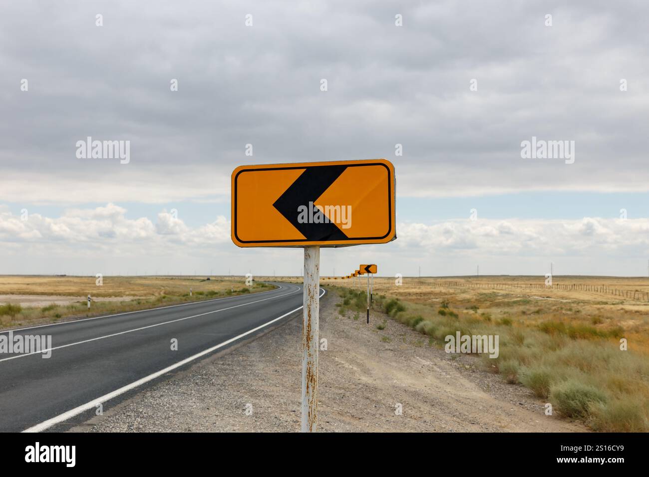 A bright yellow left turn sign stands beside a winding road in ...