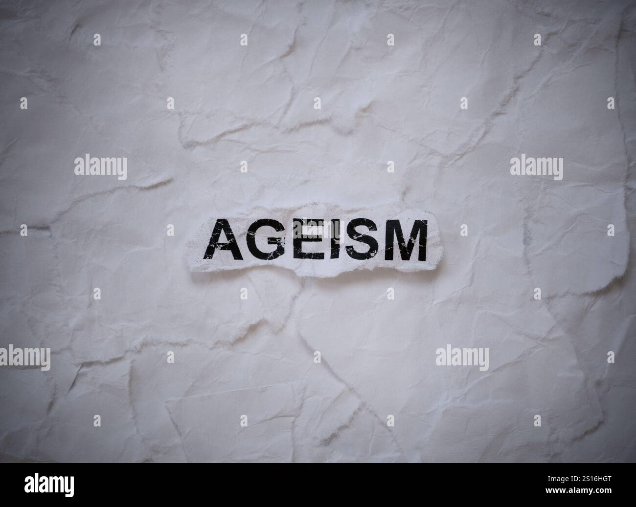Crumpled piece of paper with word Ageism on torn white paper pieces ...