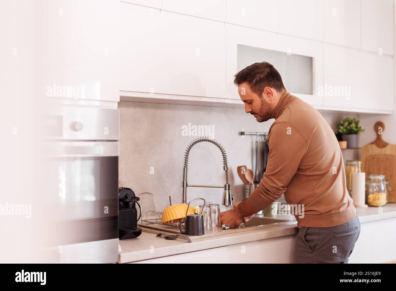 Side view of handsome mid adult man washing utensils under running ...
