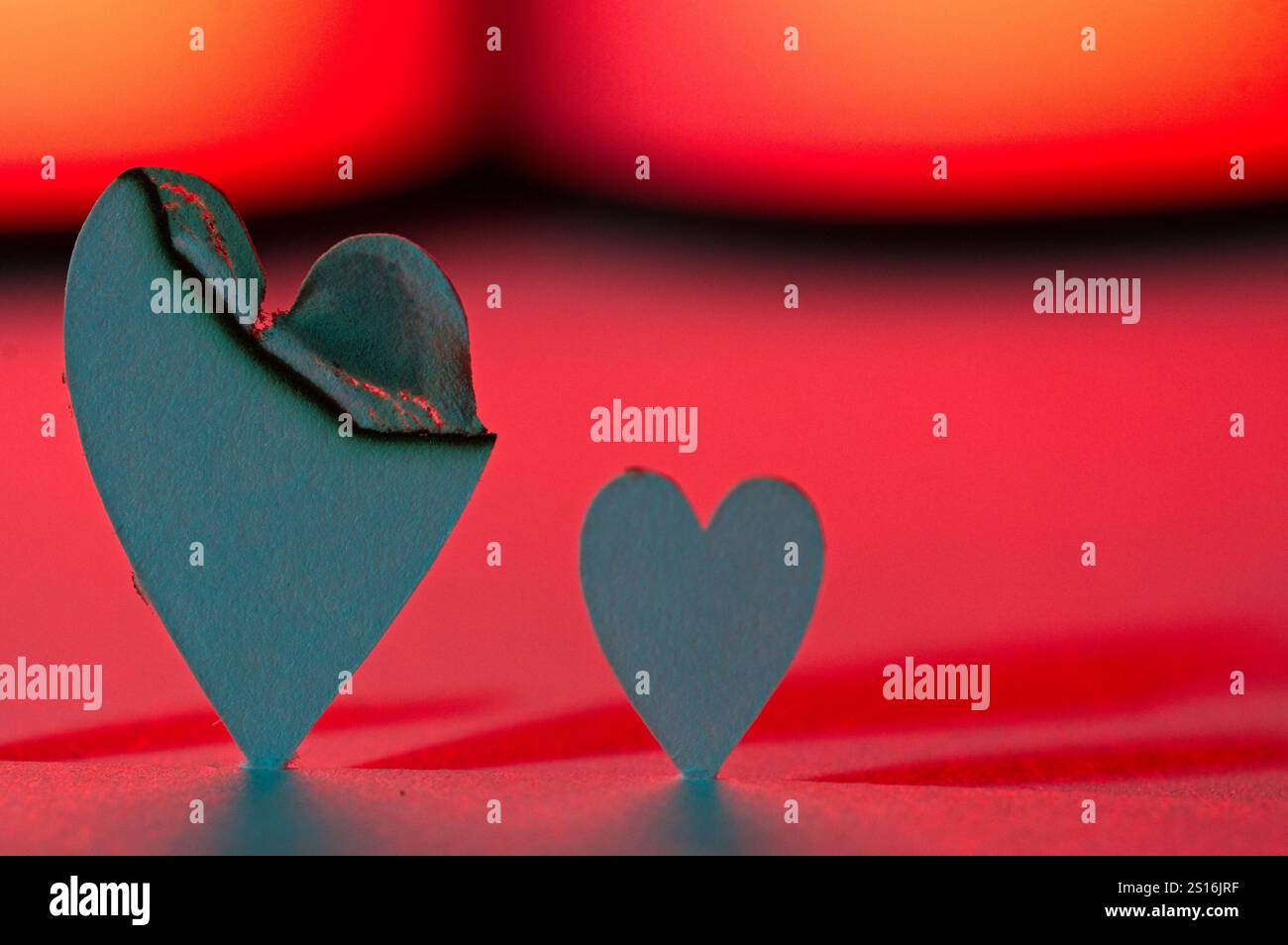 Two paper hearts on a red and pink background with shadows. One heart ...
