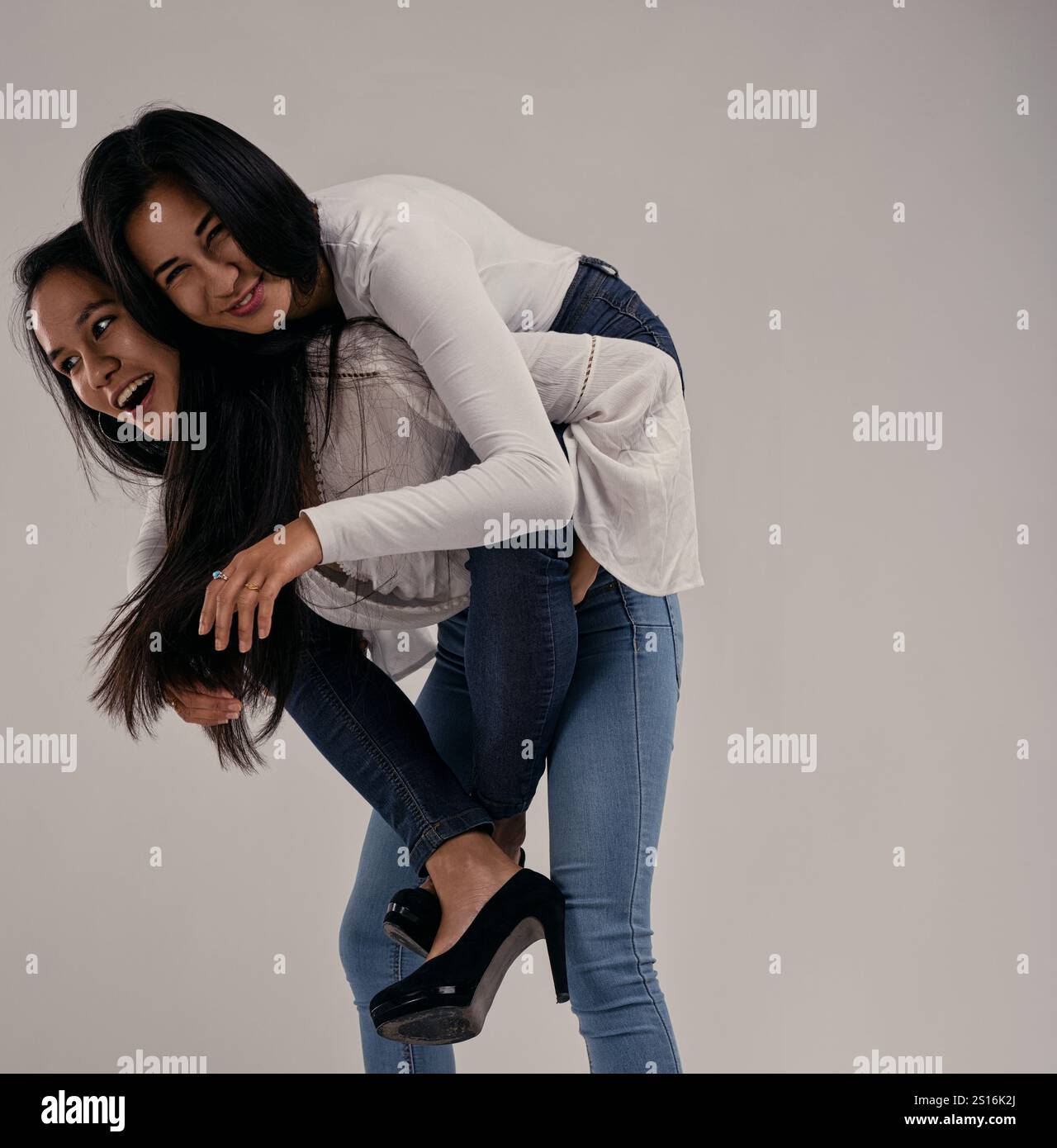 Cheerful young woman is giving a piggyback ride to her laughing friend ...