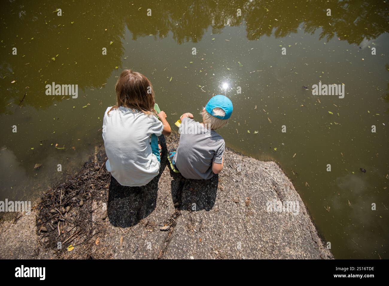 Two boys sitting by a pond Stock Photo - Alamy