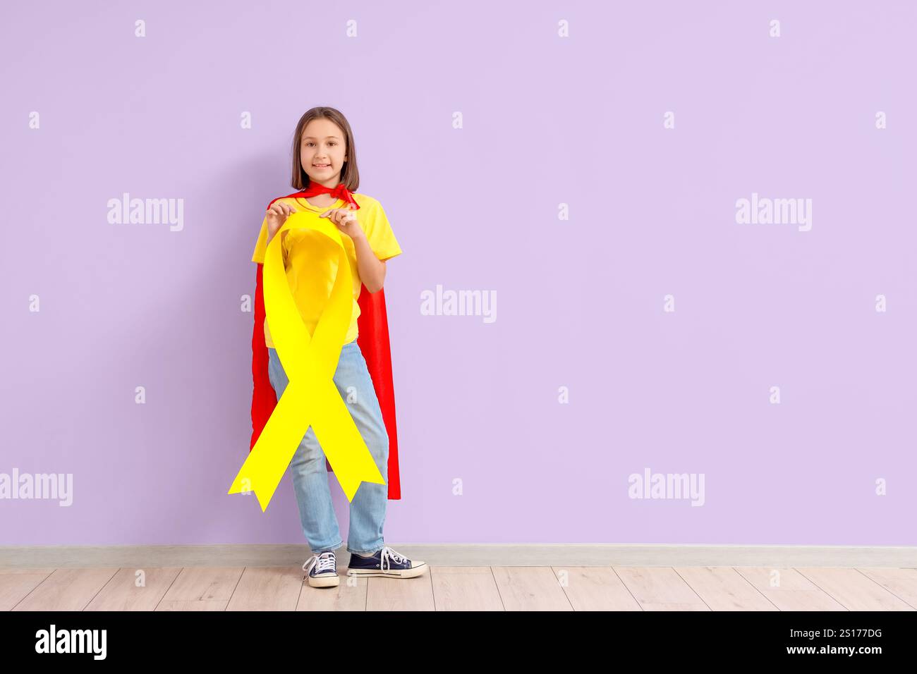 Little girl dressed as superhero with gold ribbon near lilac wall ...