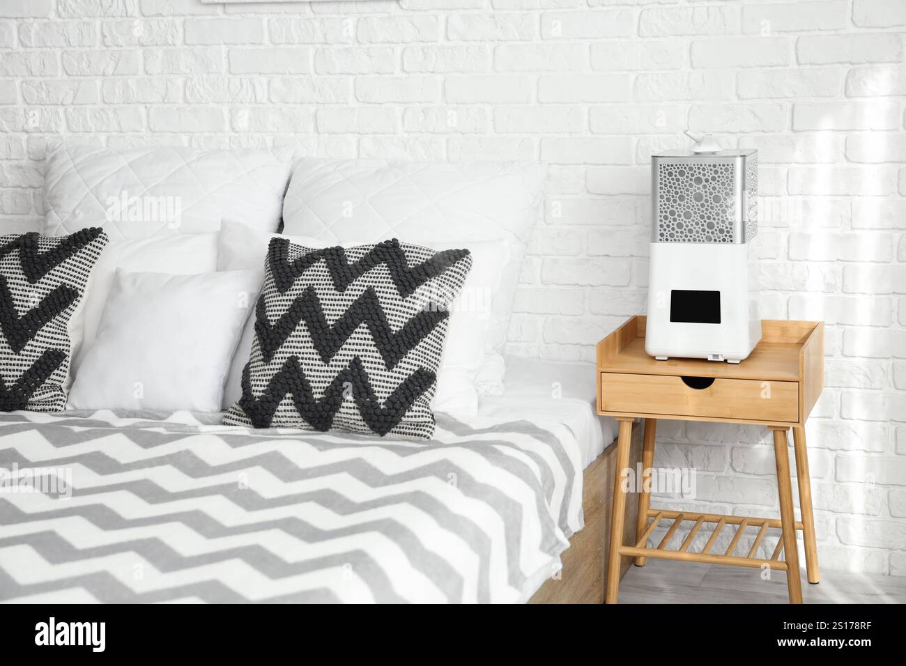 Interior of bedroom with modern humidifier on bedside table near white ...
