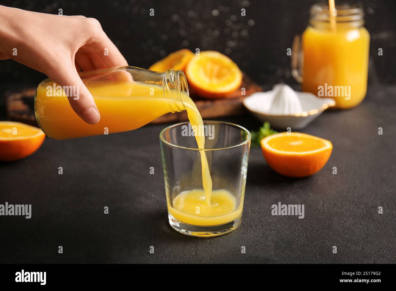 Woman pouring fresh orange juice from bottle into glass on black background Stock Photo - Alamy