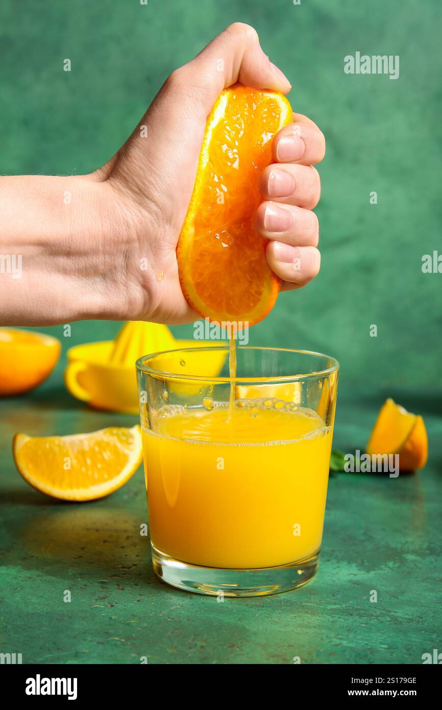 Female hand squeezing orange juice into glass on green background Stock ...