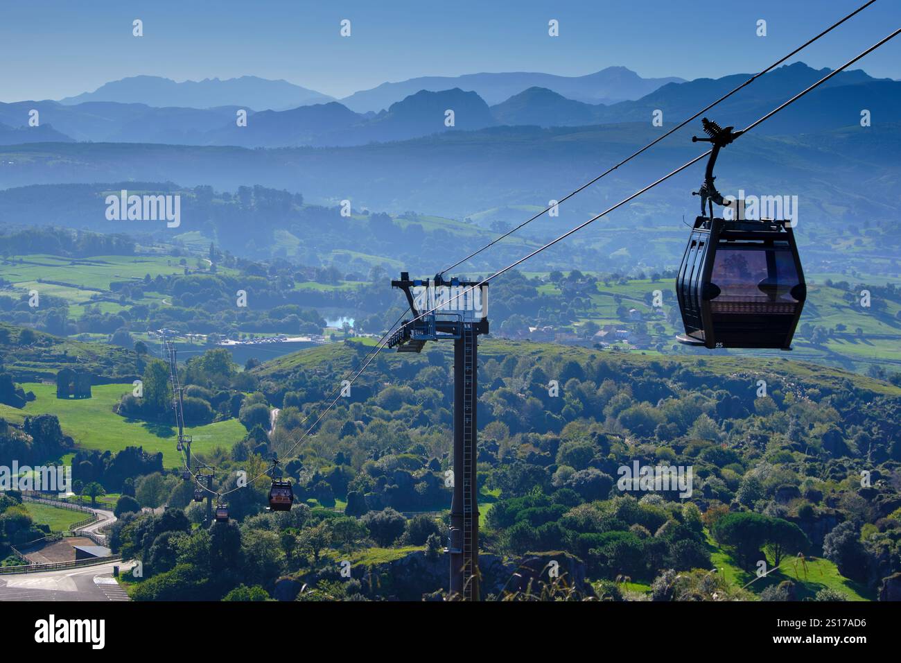 A cable car is suspended above a lush green valley. The cable car is ...