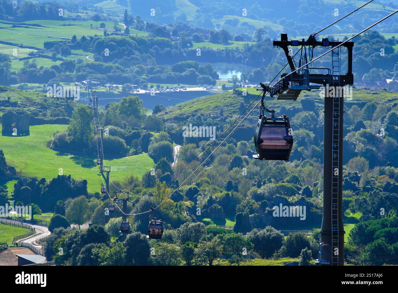 A cable car is suspended above a lush green valley. The cable car is ...