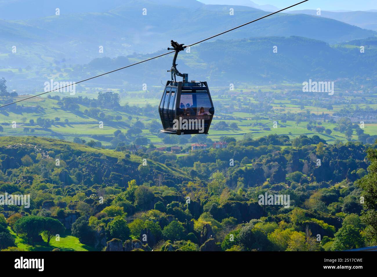 A cable car is suspended above a lush green valley. The cable car is ...