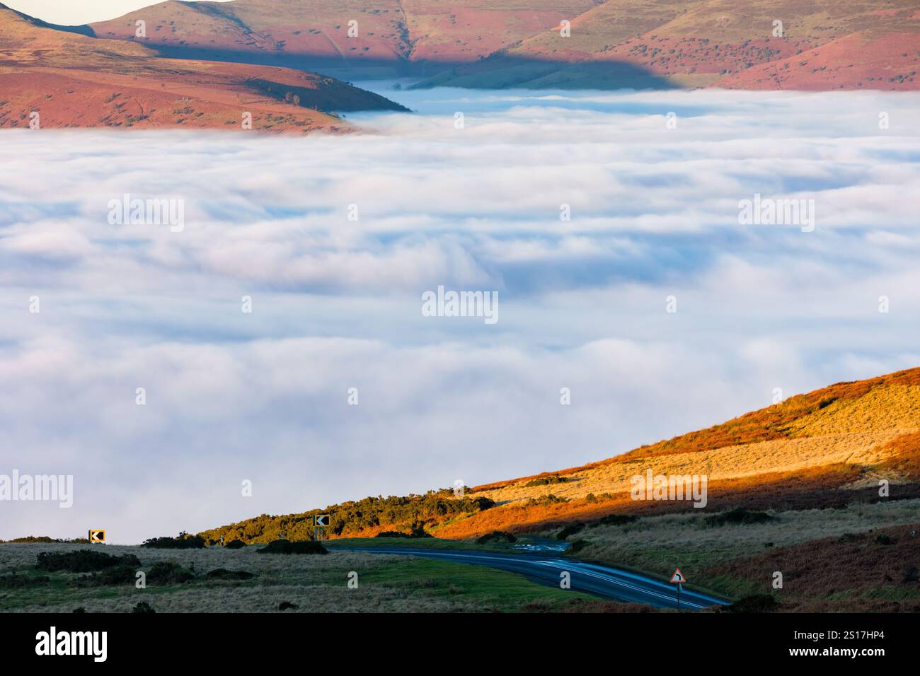 Small, winding rural road leading towards a fog filled valley below ...