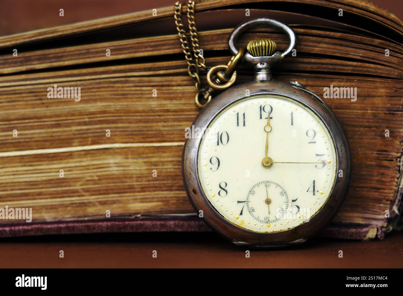 An antique pocket watch leans against an old book with yellowed pages ...