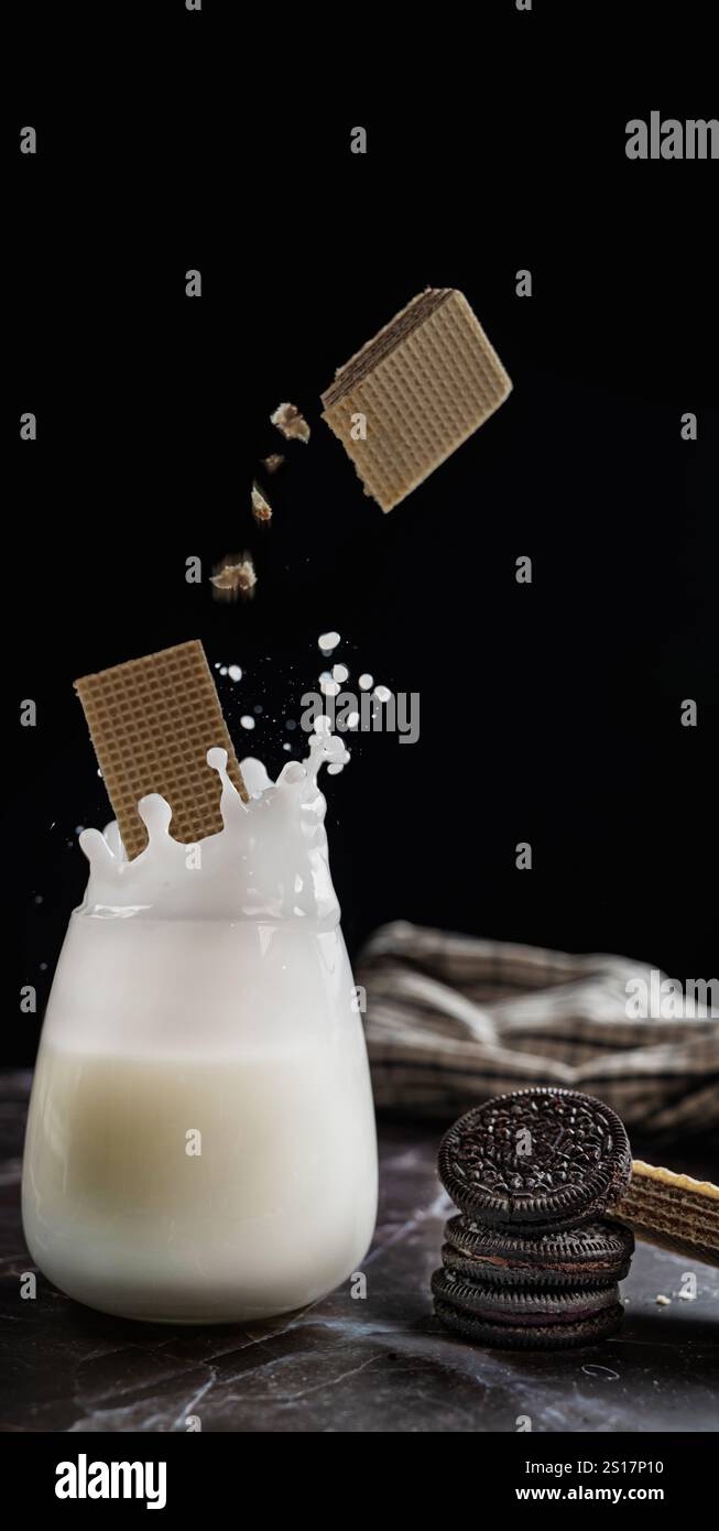 Milk Splash from biscuit fall in the glass on a black background. Dairy ...