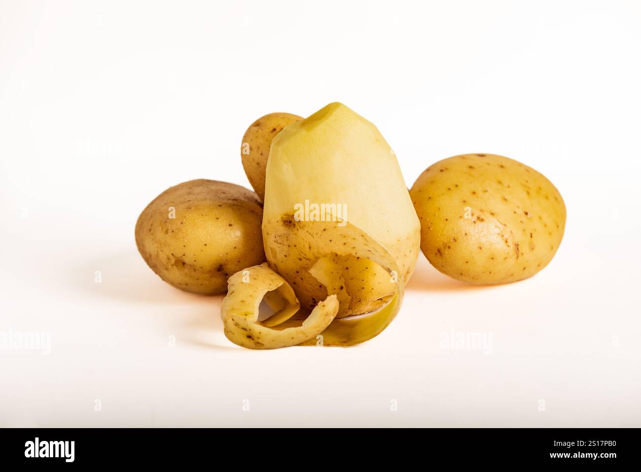 Raw potatoes, one of them half-peeled, exposing the interior of the ...