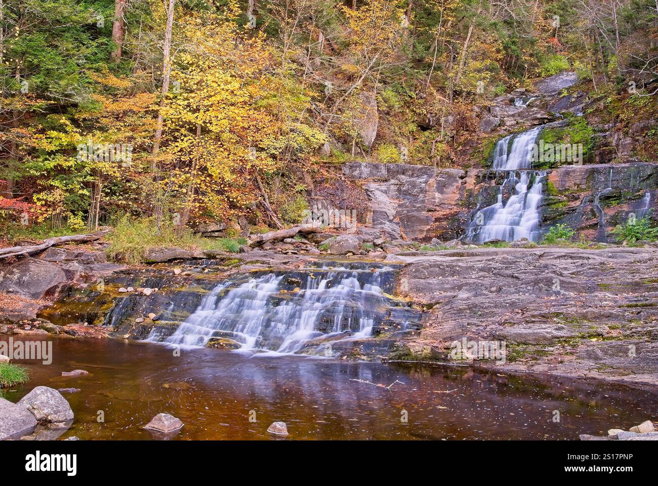 Flowing waters cascade down series of waterfalls framed by autumn trees ...