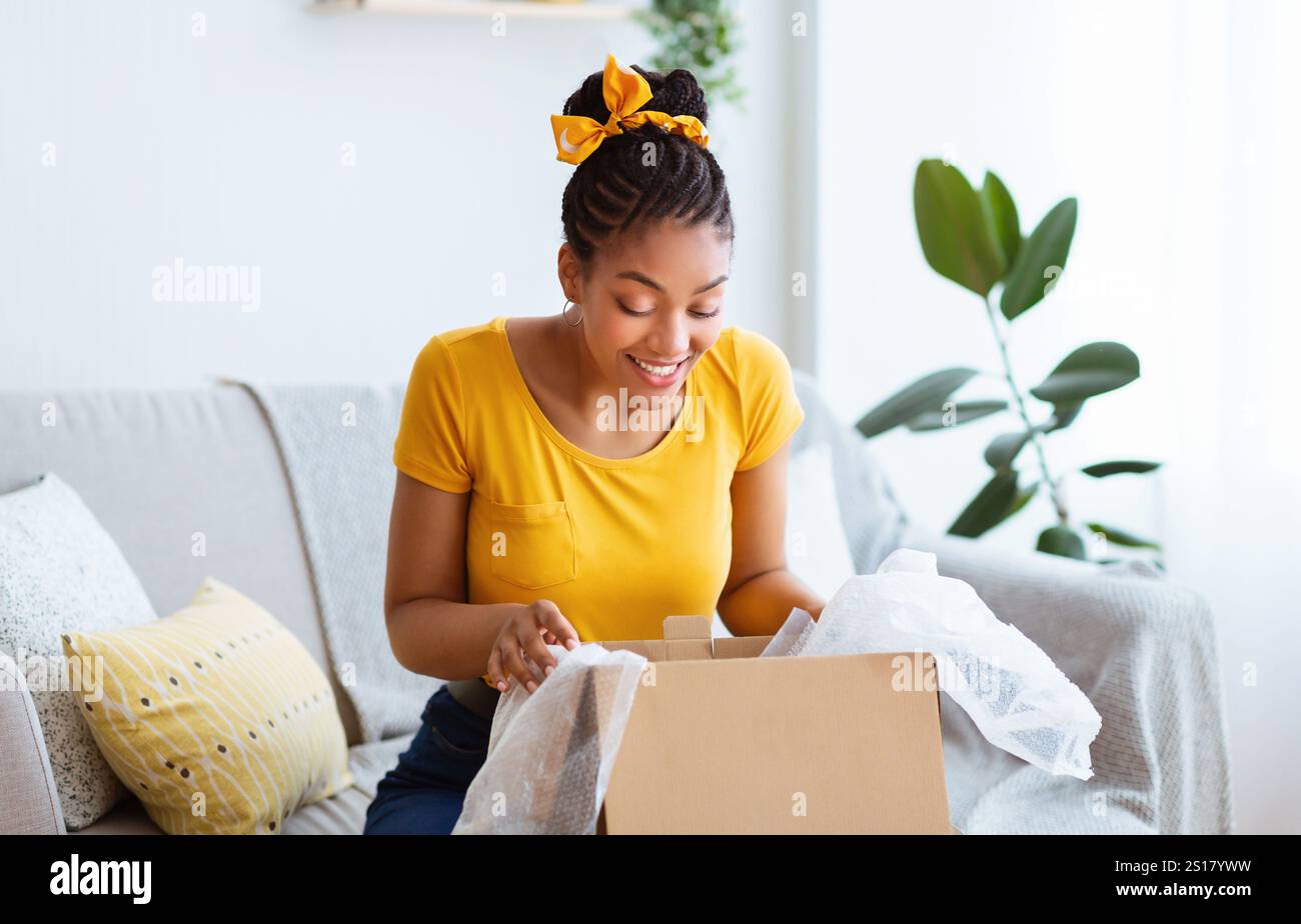 Excited black woman unpacking box after online shopping Stock Photo - Alamy