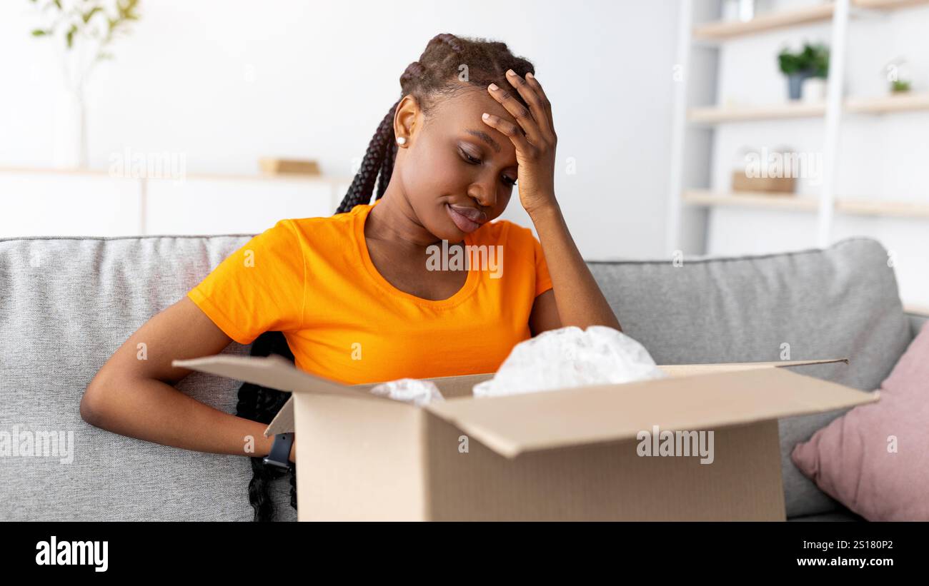 Disappointed black woman unboxing her delivery, looking inside wrong box, touching her forehead ...