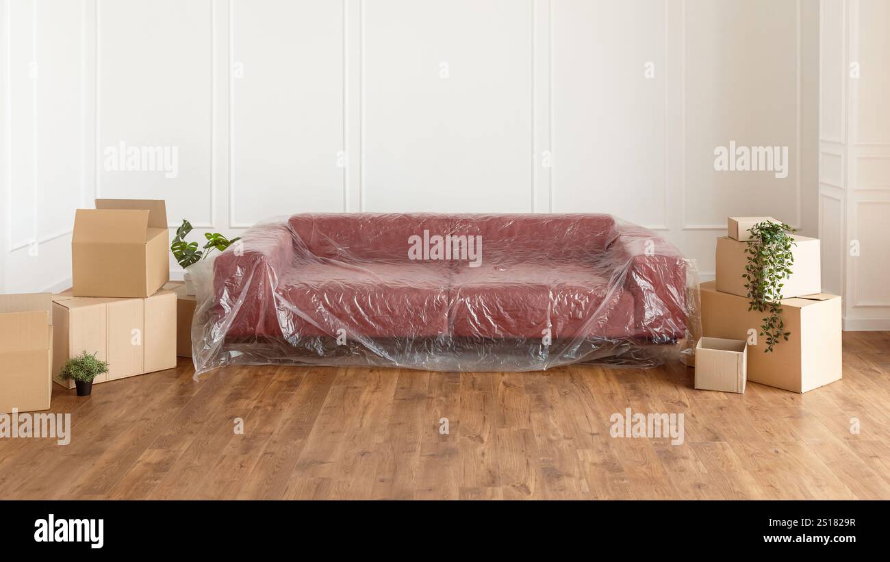 Living room with covered sofa, stacks of boxes during relocation Stock ...