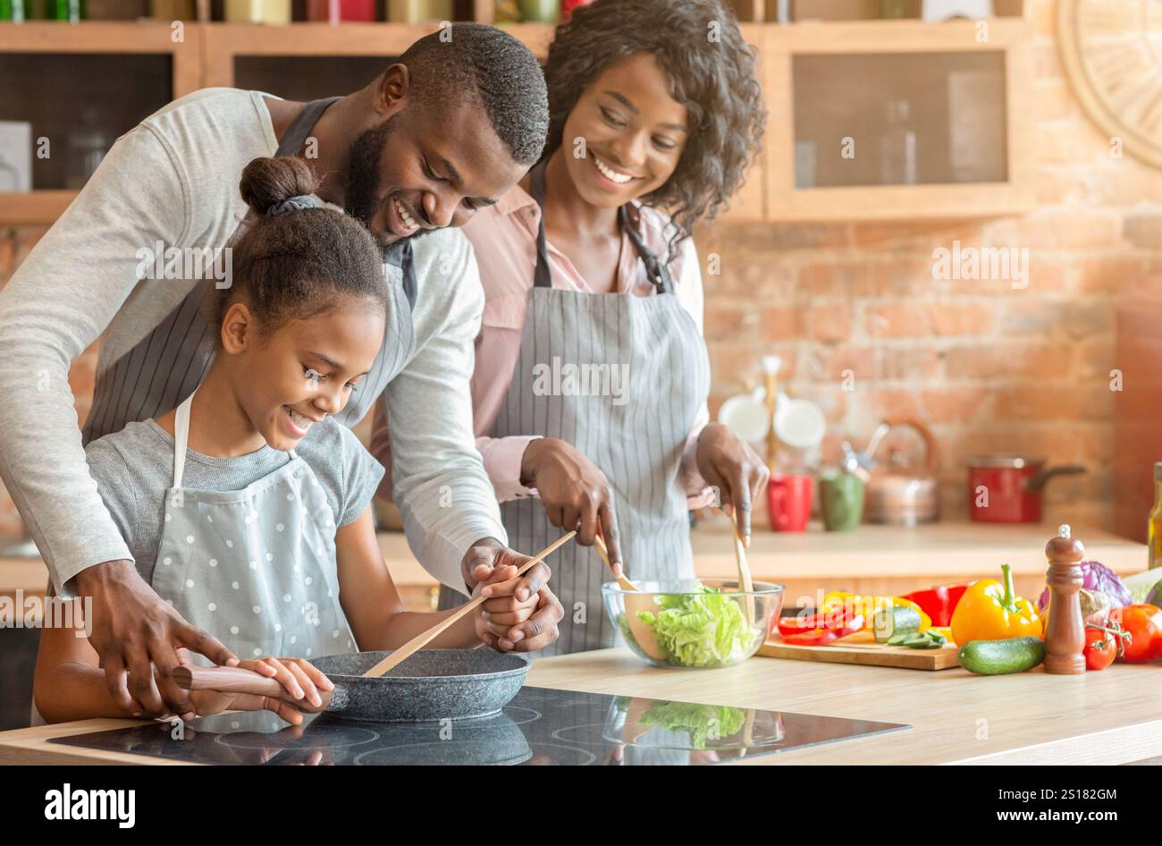 Afro parents teaching their daughter how to cook Stock Photo - Alamy