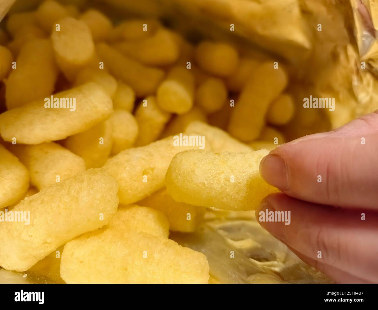 Hand reaches into a shimmering bag filled with fluffy, golden snacks ...