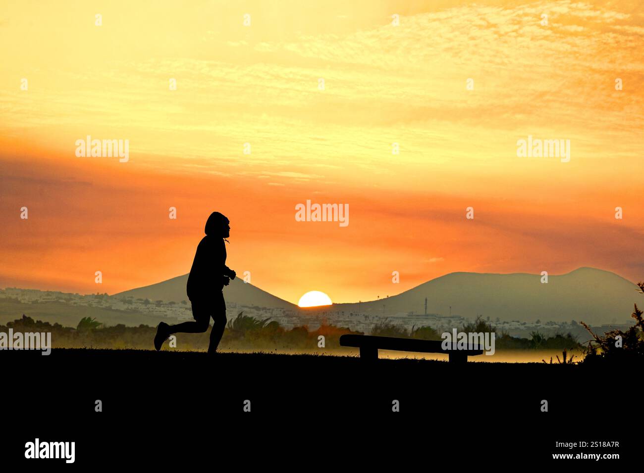 Early misty morning male runner with hoody top against red sky and sun rising between mountains ...