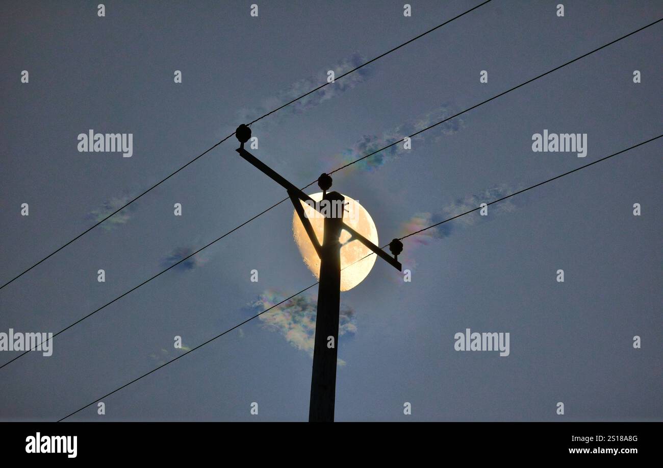 Telegraph power lines comms cables against illuminated half moon and ...