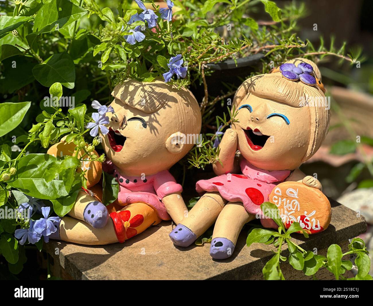 Two delightful clay dolls are sitting side by side on a wooden block ...