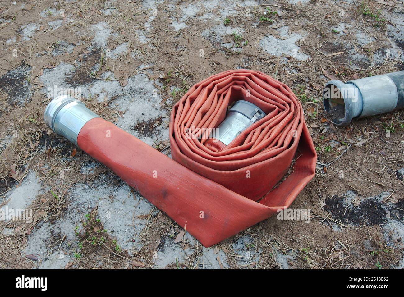 Close up of a curled up red discharge hose on the ground in dirt and ...