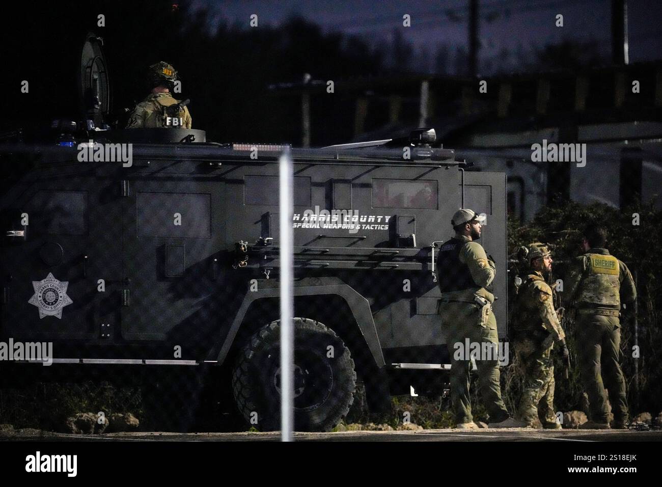 Law enforcement officers stand behind a SWAT vehicle near a location in ...