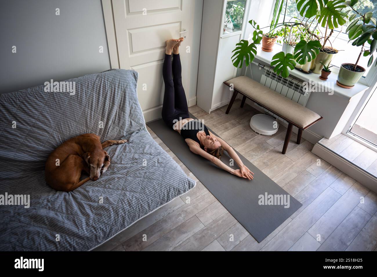 Spiritual woman lies on yoga mat with feet against door, arms stretched ...