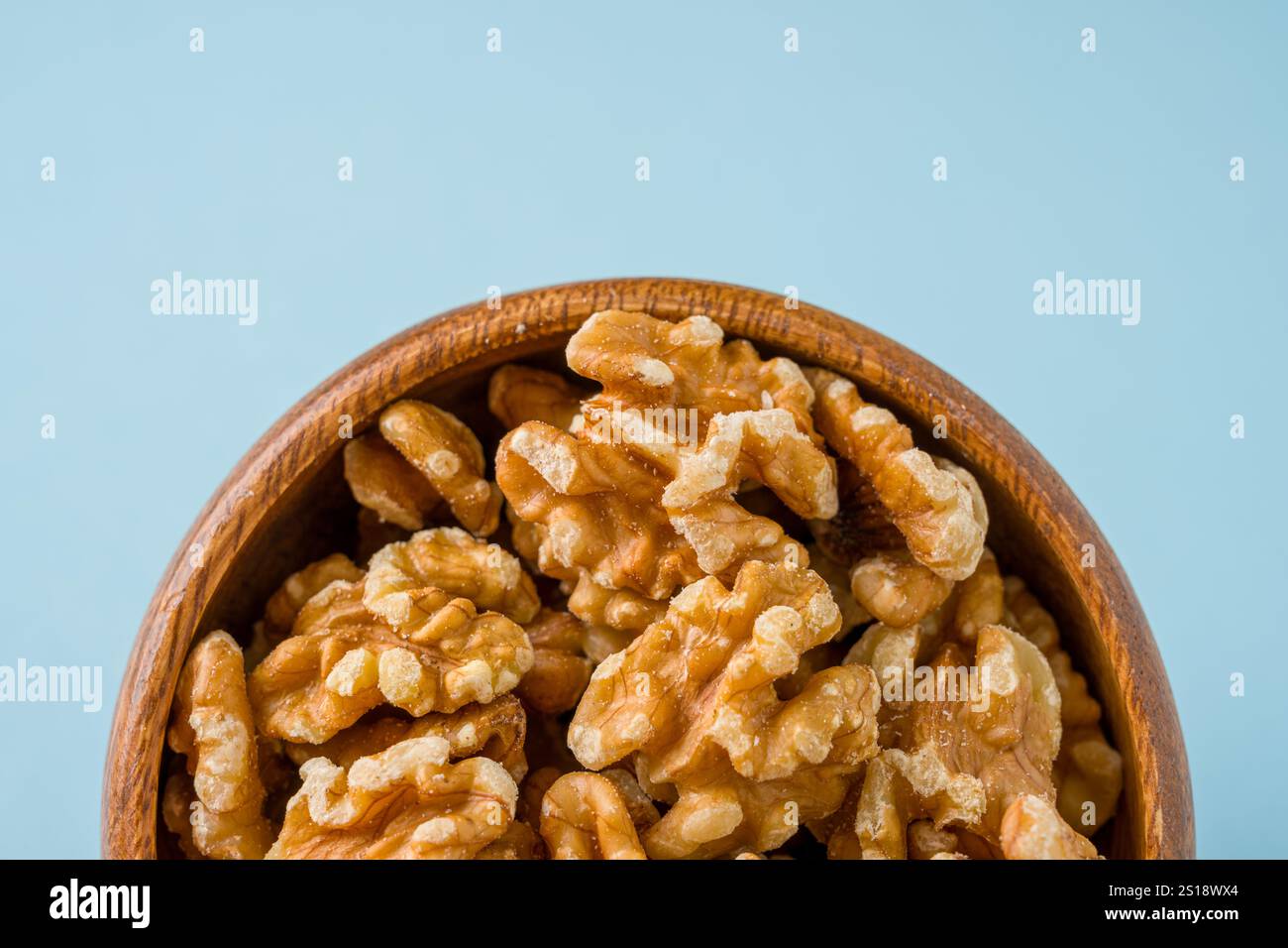Top view of heap of walnut kernels in wooden bowl on blue background ...