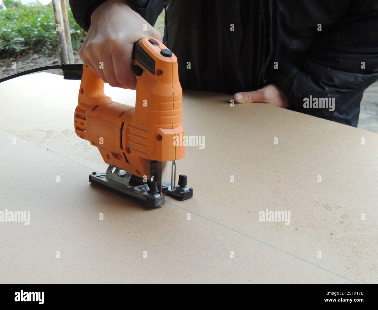 worker's hand in dark jacket holds orange corded jigsaw over marked ...