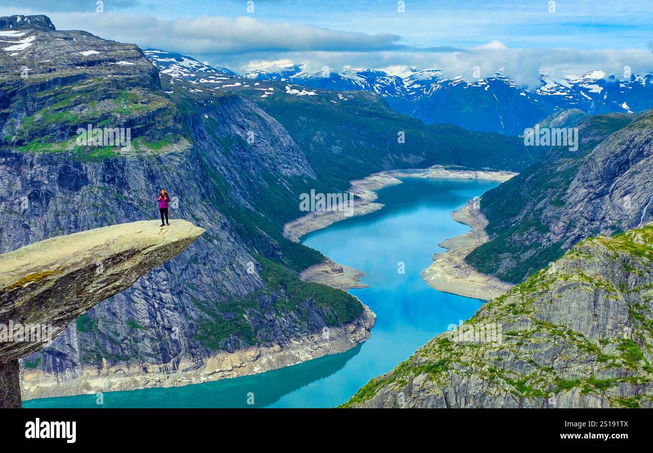 A lone adventurer stands atop the iconic Trolltunga, gazing over ...