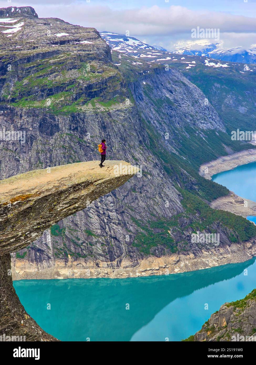A lone adventurer stands atop the iconic Trolltunga, gazing over ...