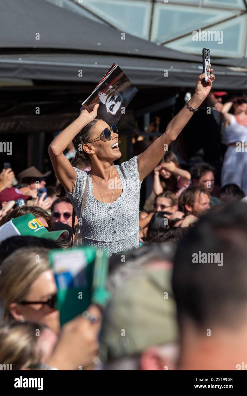 A fan rides on shoulders above the crowd as she waves a photo of Robbie ...