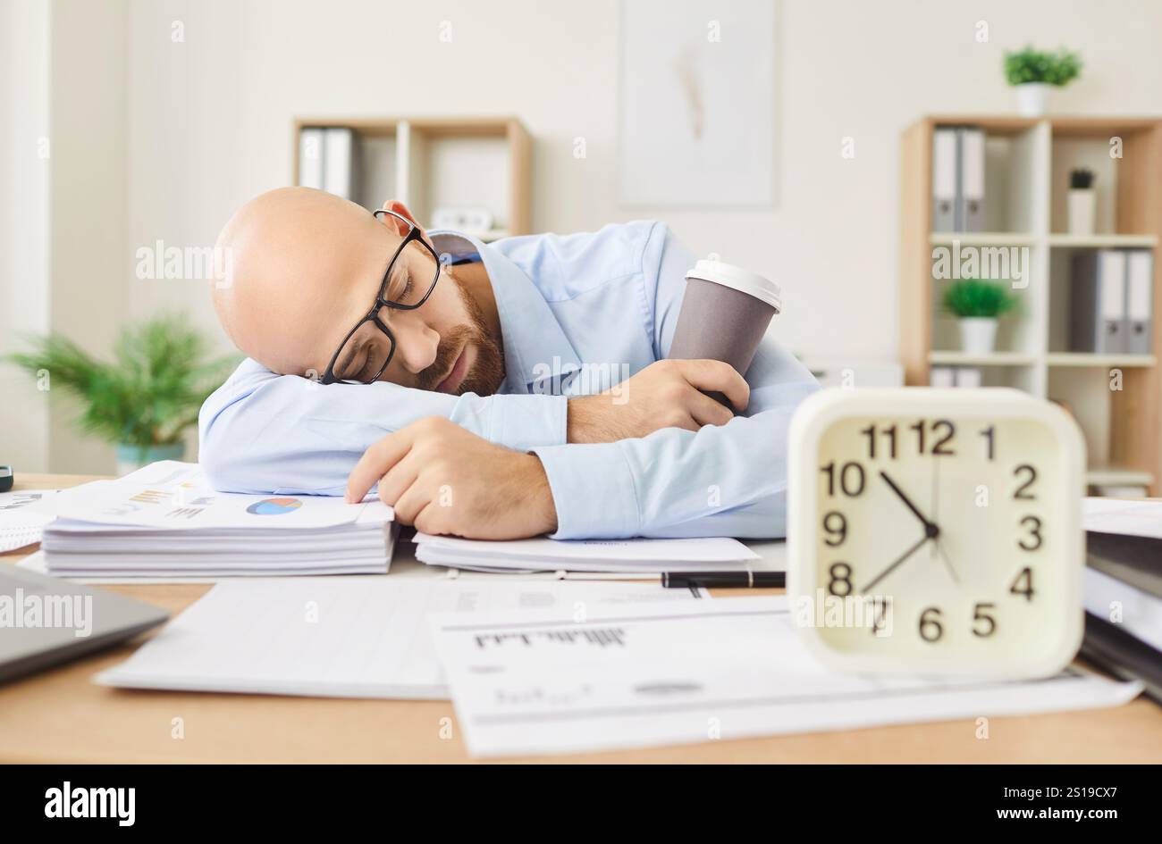 Exhausted Man Sleeping At Desk Holding Coffee Amidst Office Documents ...