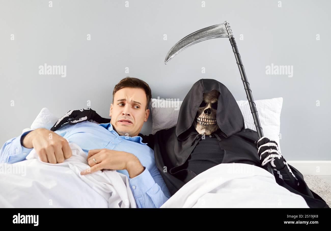 Shocked scared man lying on bed with skeleton in a grim reaper death ...