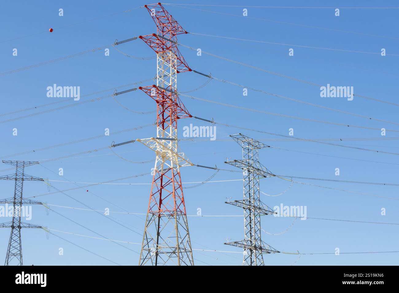 Red and white metallic electricity pylons transporting high voltage ...
