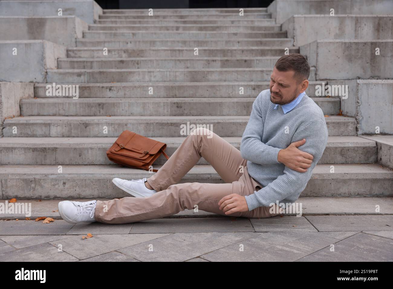 Man with injured arm on stairs outdoors after fall. Dangerous accident ...