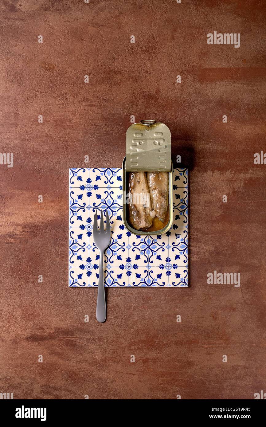 Open tin of sardine fillets in oil, served with fork on white-and-blue ...
