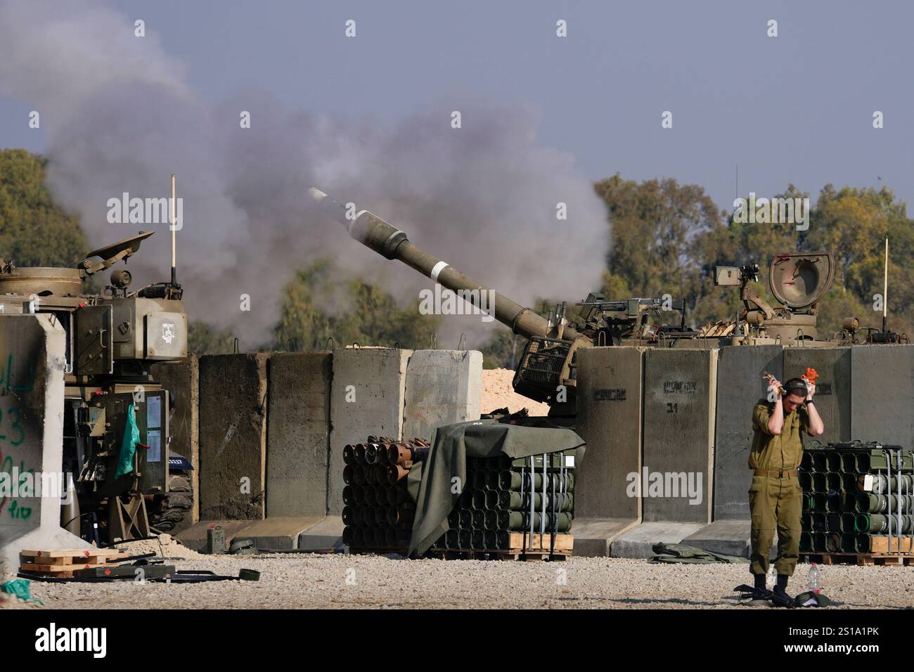 An Israeli soldier covers his ears as an artillery gunner fires into ...