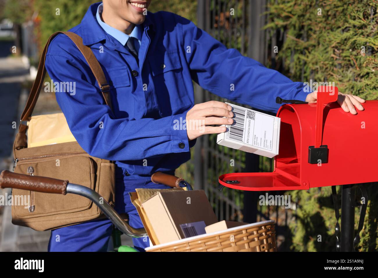 Postman with bicycle putting parcel into mail box outdoors, closeup ...