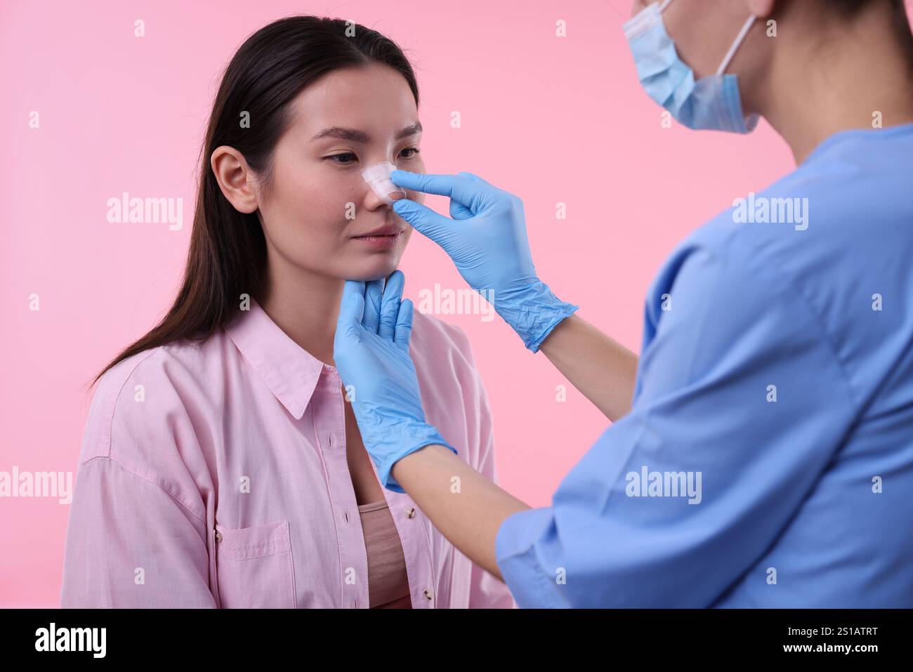 Doctor checking patient's nose after plastic surgery operation on pink ...