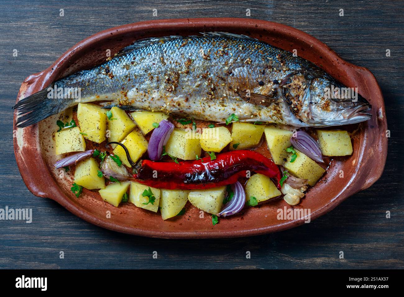 Delicious baked big sea bass fish with spices in a clay plate and fried ...